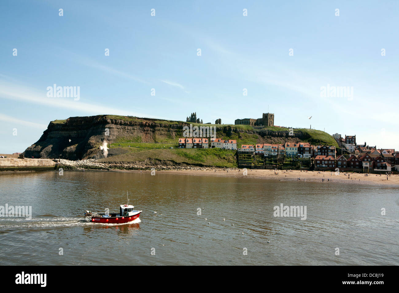 A small fishing boat entering Whitby harbor, a small beach, houses and ...