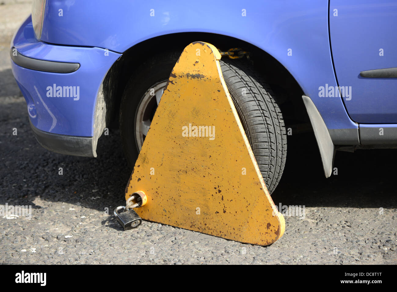 Closeup of a yellow wheel clamp attached to a blue car for a parking ...