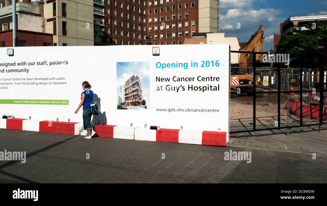 A woman walking past sign on hoarding announcing 2016 Opening of the ...
