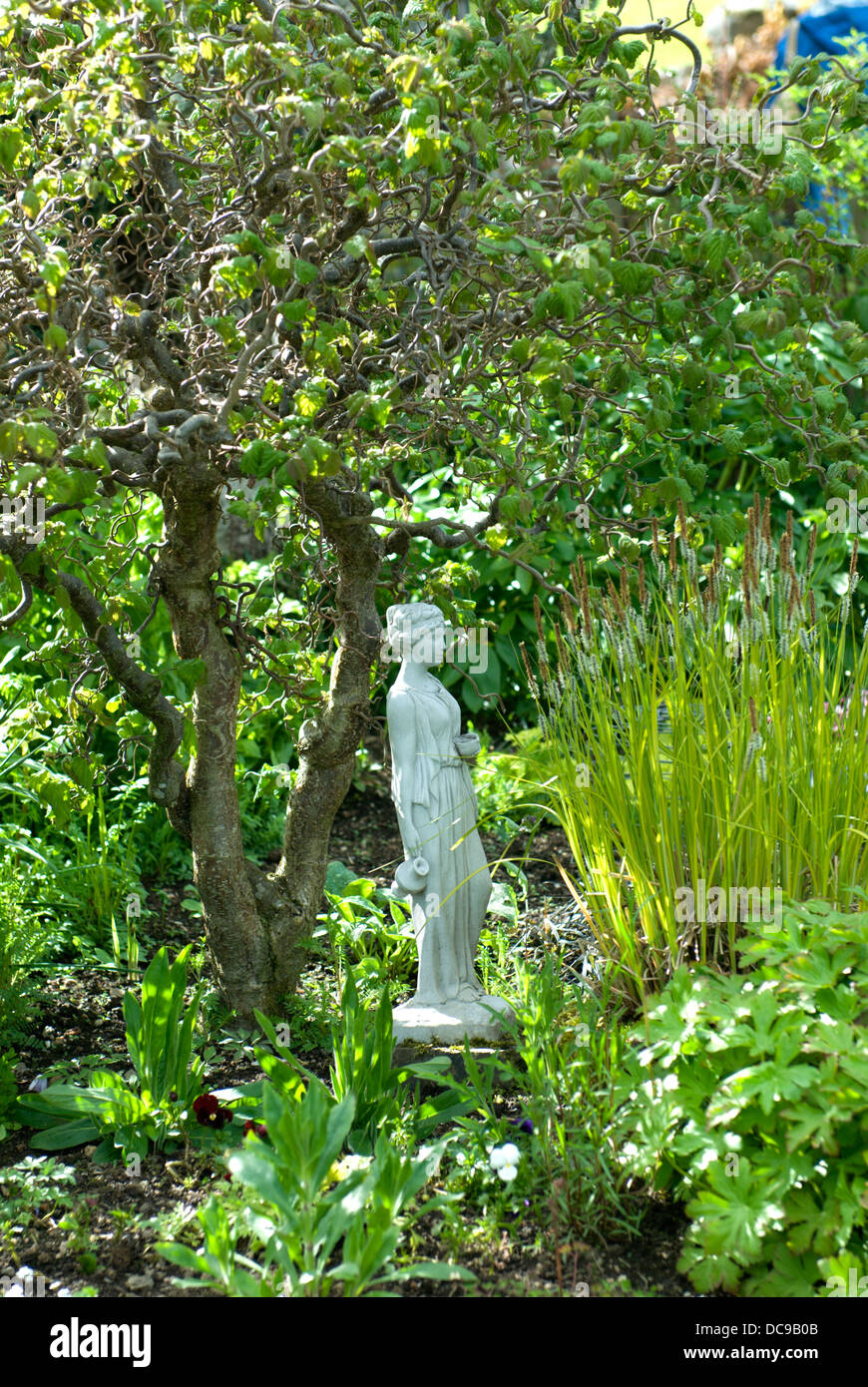 A statue almost hidden in the fresh green spring growth of a garden ...