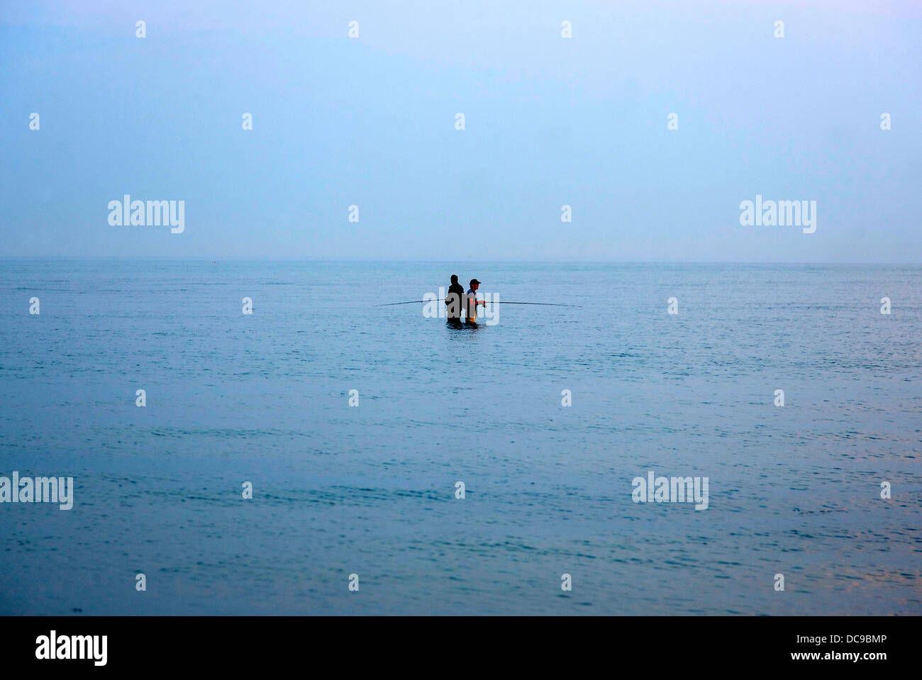 Two fishermen back to back, sea fishing Stock Photo - Alamy