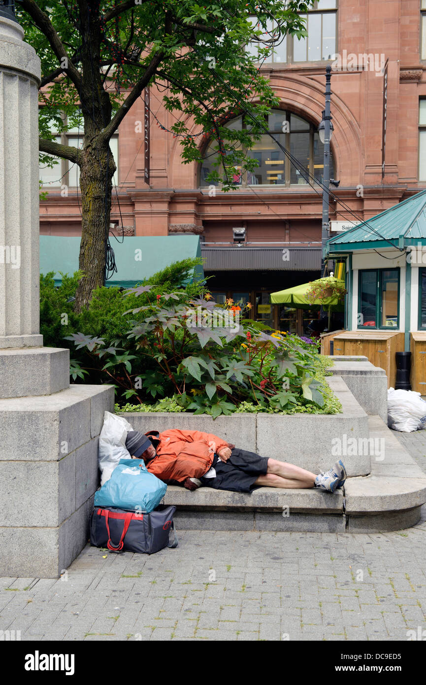 Homeless man sleeping on a concrete bench in downtown Montreal Stock ...