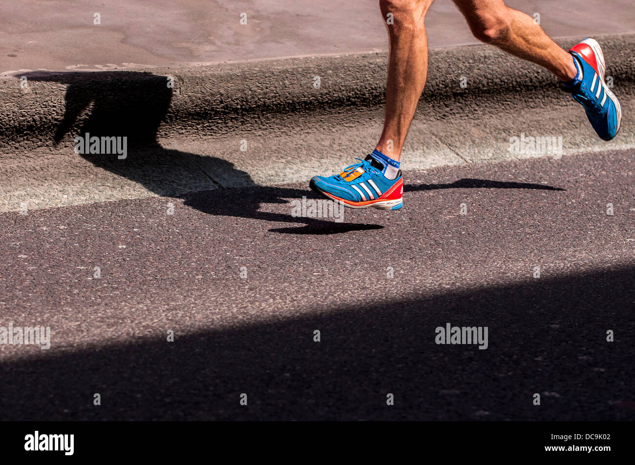 Athlete taking part in a race running by with shadow falling on to the ...