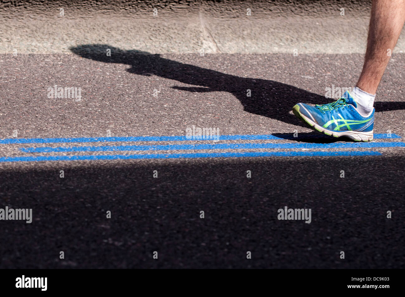 Athlete taking part in a race running by with shadow falling on to the ...
