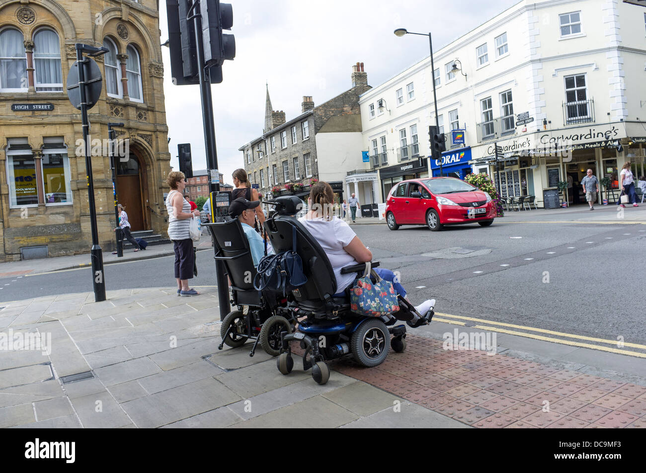 Disabled people in electric powered wheelchairs waiting to cross road ...