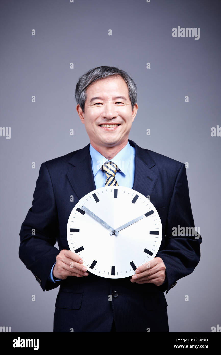 middle aged man in a business suit holding a clock Stock Photo - Alamy