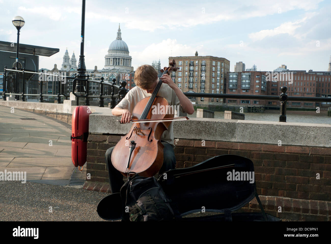 A young man busker playing the classical music on the cello with a view ...