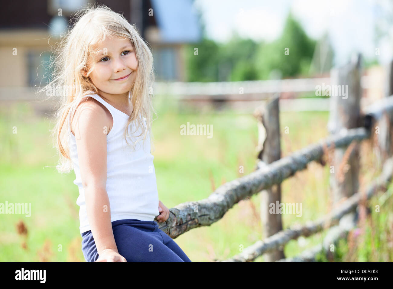 Pretty little girl in white singlet sitting on fence. Copyspace ...