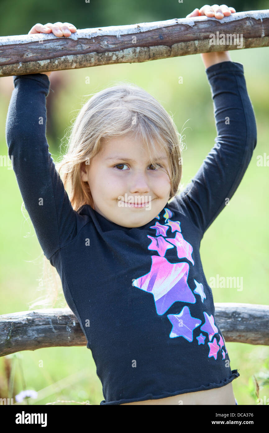 Hanging at hands on log beautiful little girl, summer day. Russian ...