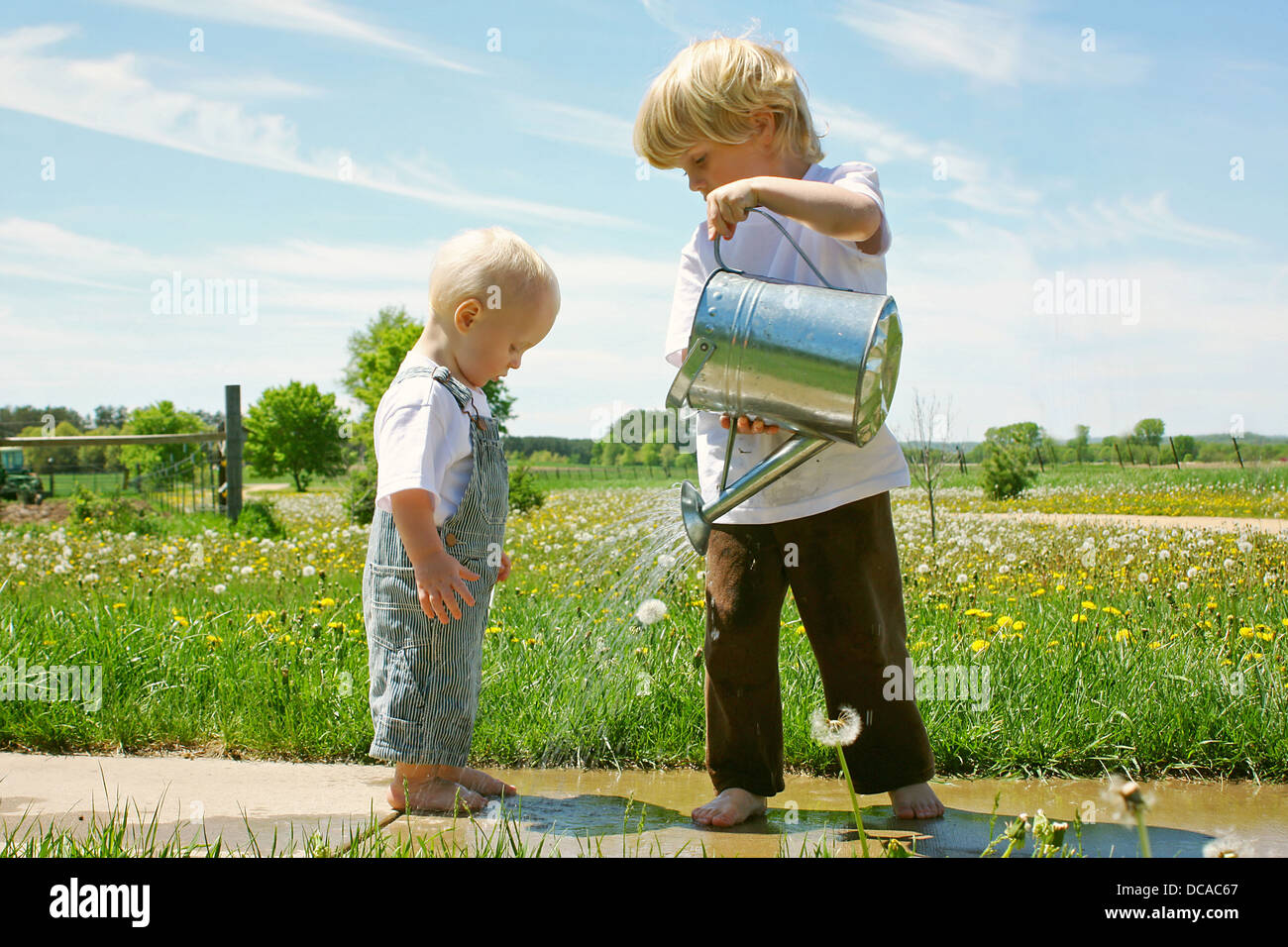 A young child is watering the feet of his baby brother on a sunny ...