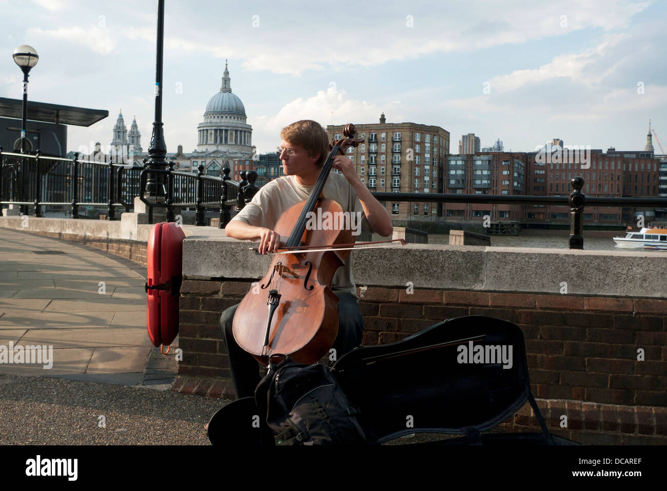 A young man musician busker playing classical music on the cello with a ...