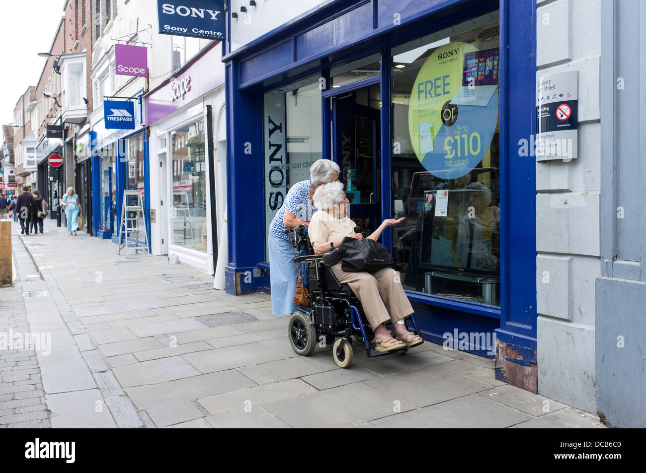 Elderly disabled lady in electric wheelchair with friend looking at TV ...