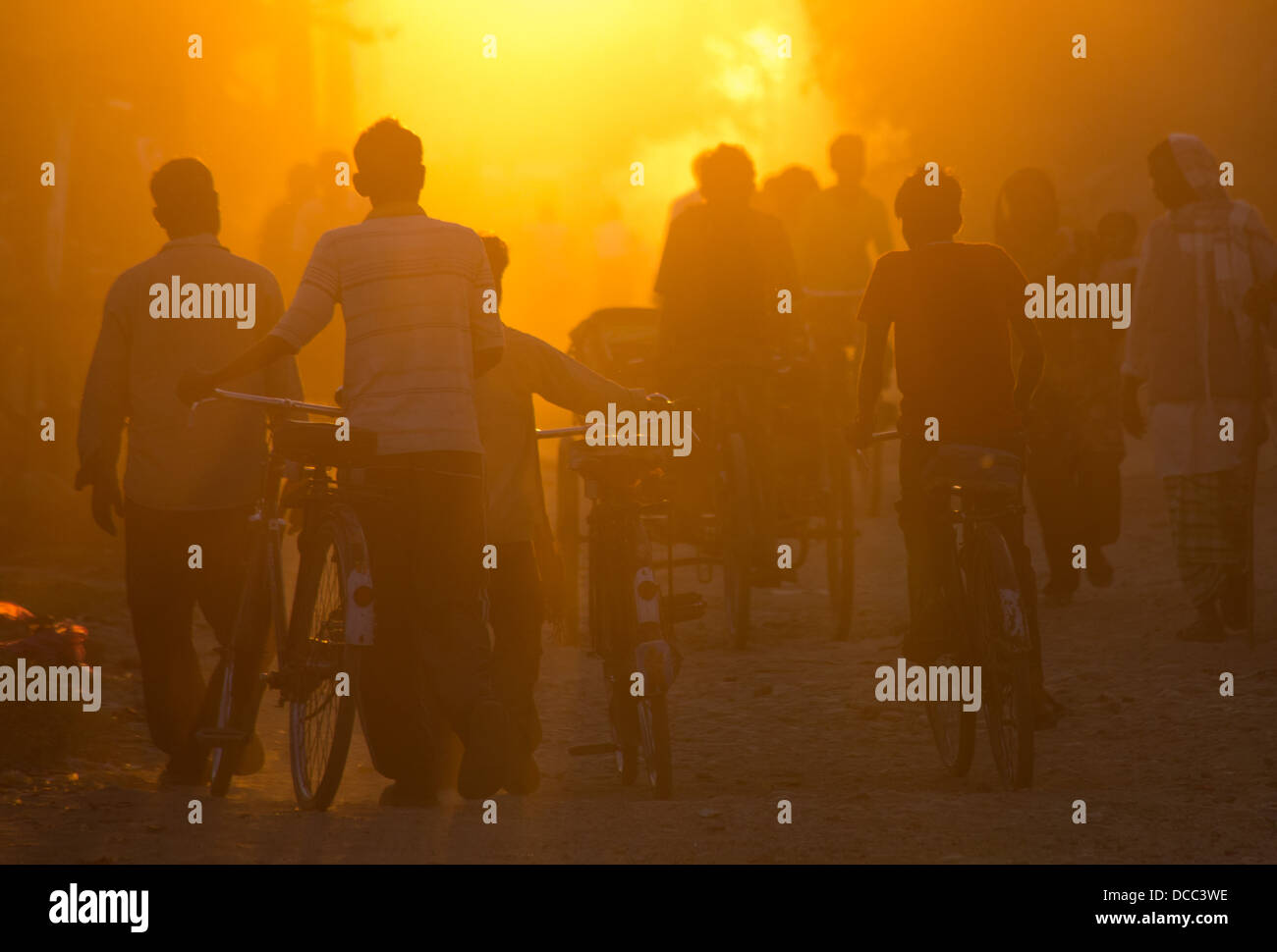 Busy street scene at sunset with silhouettes of people and bicycles ...