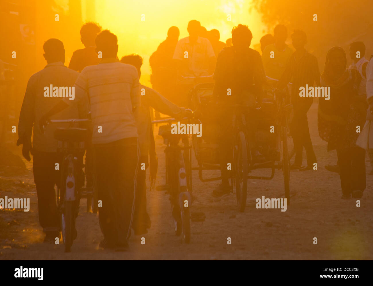 Busy street scene at sunset with silhouettes of people and bicycles ...