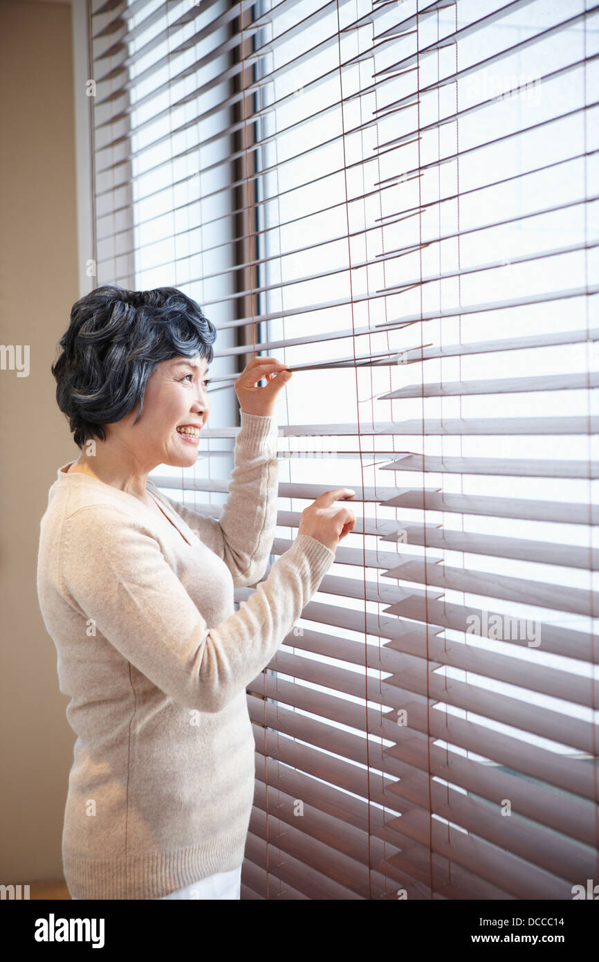 middle aged woman looking out through wooden blinds Stock Photo - Alamy