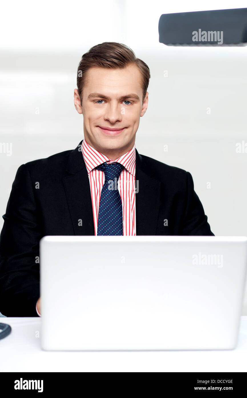 Attractive smiling man operating a laptop isolated against white ...