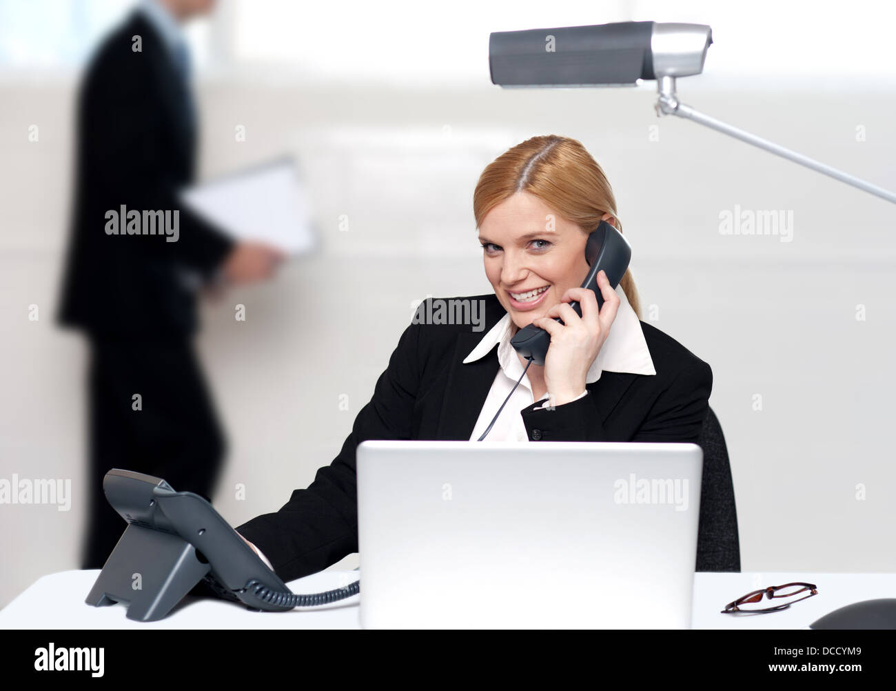 Attractive secretary attending phone call while man walk by in ...
