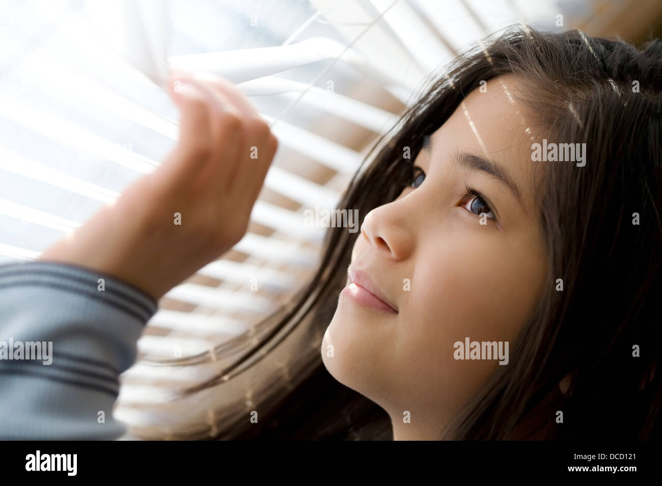 Girl looking out window through blinds Stock Photo - Alamy