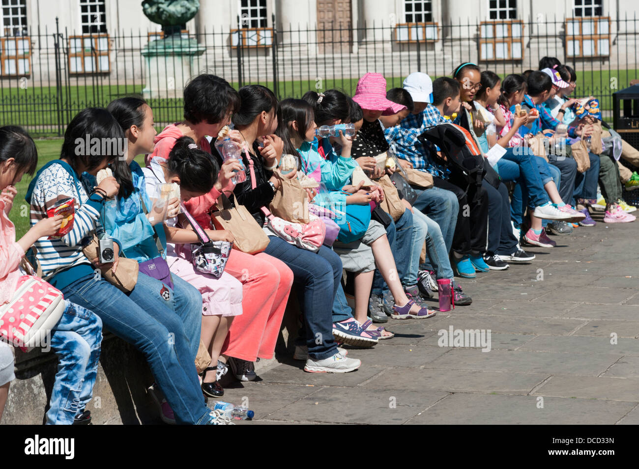A line of young Chinese children tourists eating lunch on a wall in ...