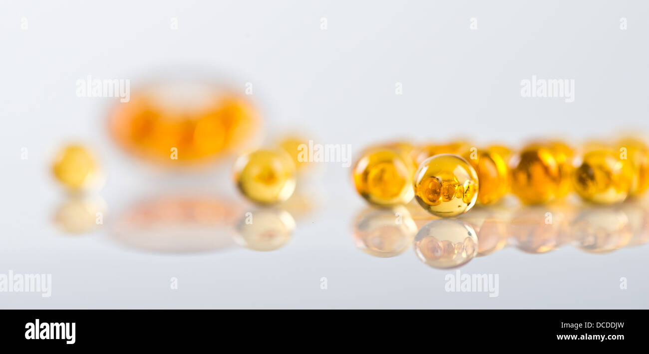 Capsules of fish oil spilled out open container Stock Photo - Alamy