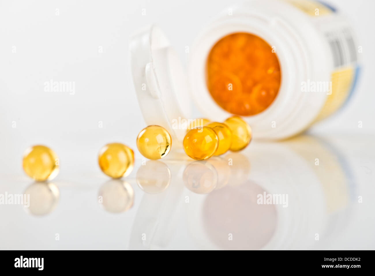 Capsules of fish oil spilled out open container Stock Photo - Alamy