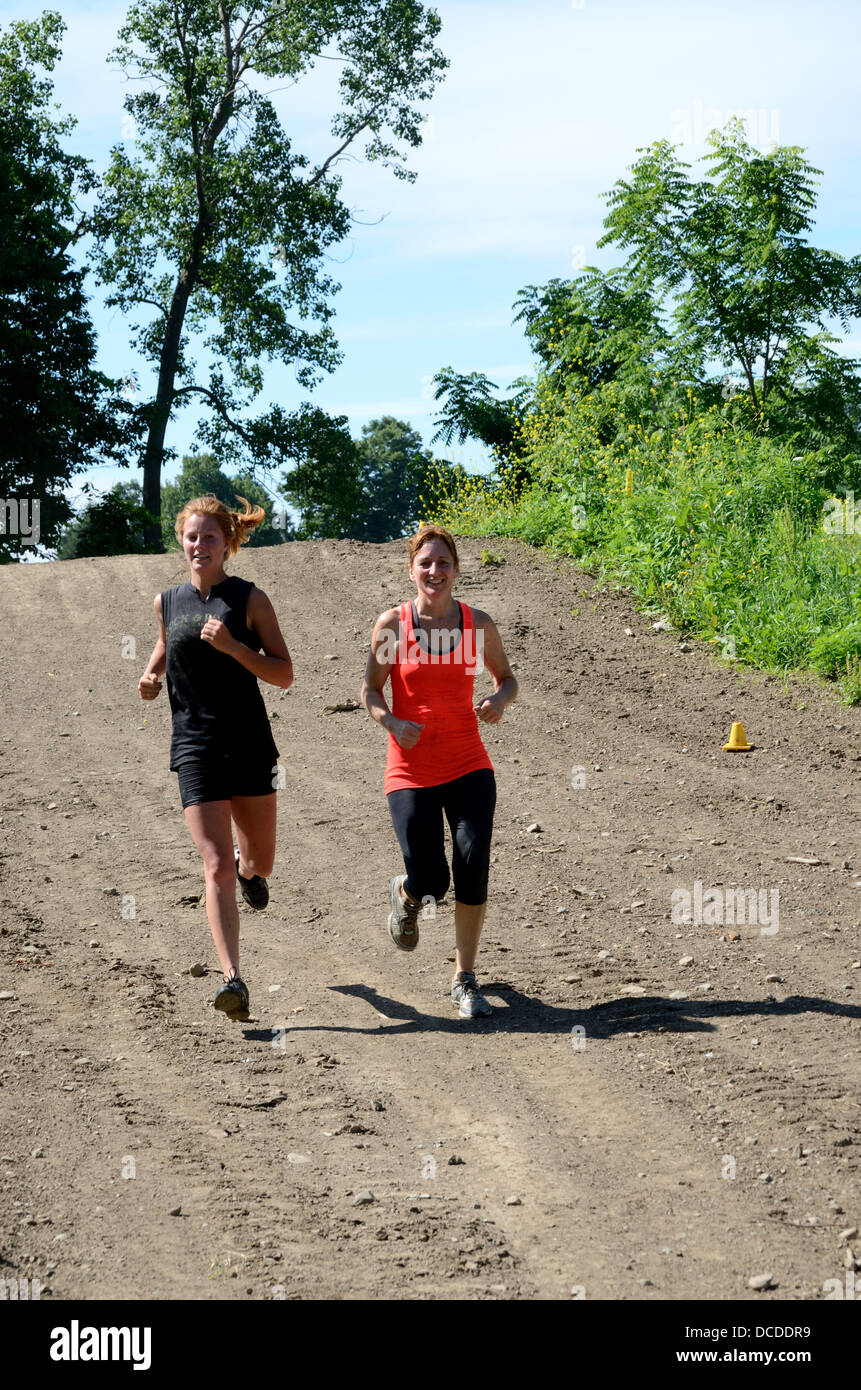 Two women runners descend hill in 5K mud run Stock Photo - Alamy