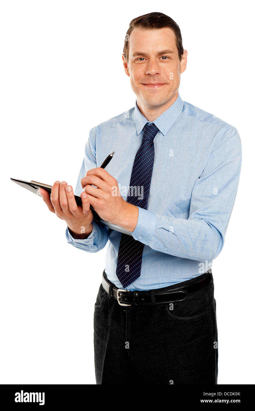 Male secretary taking down notes from boss on notepad looking at camera ...