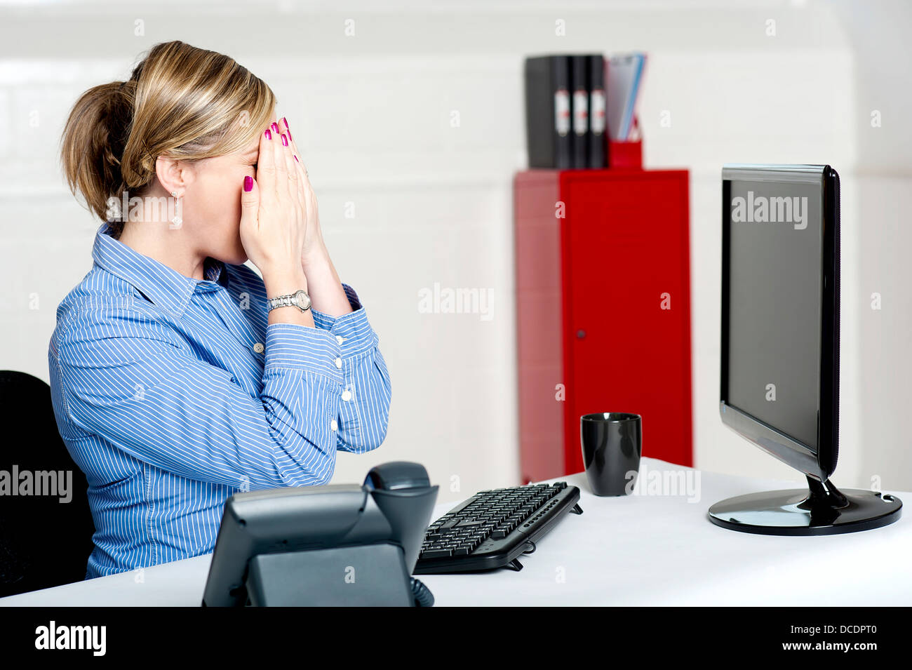 Female secretary hiding her face with hands sitting in front of ...