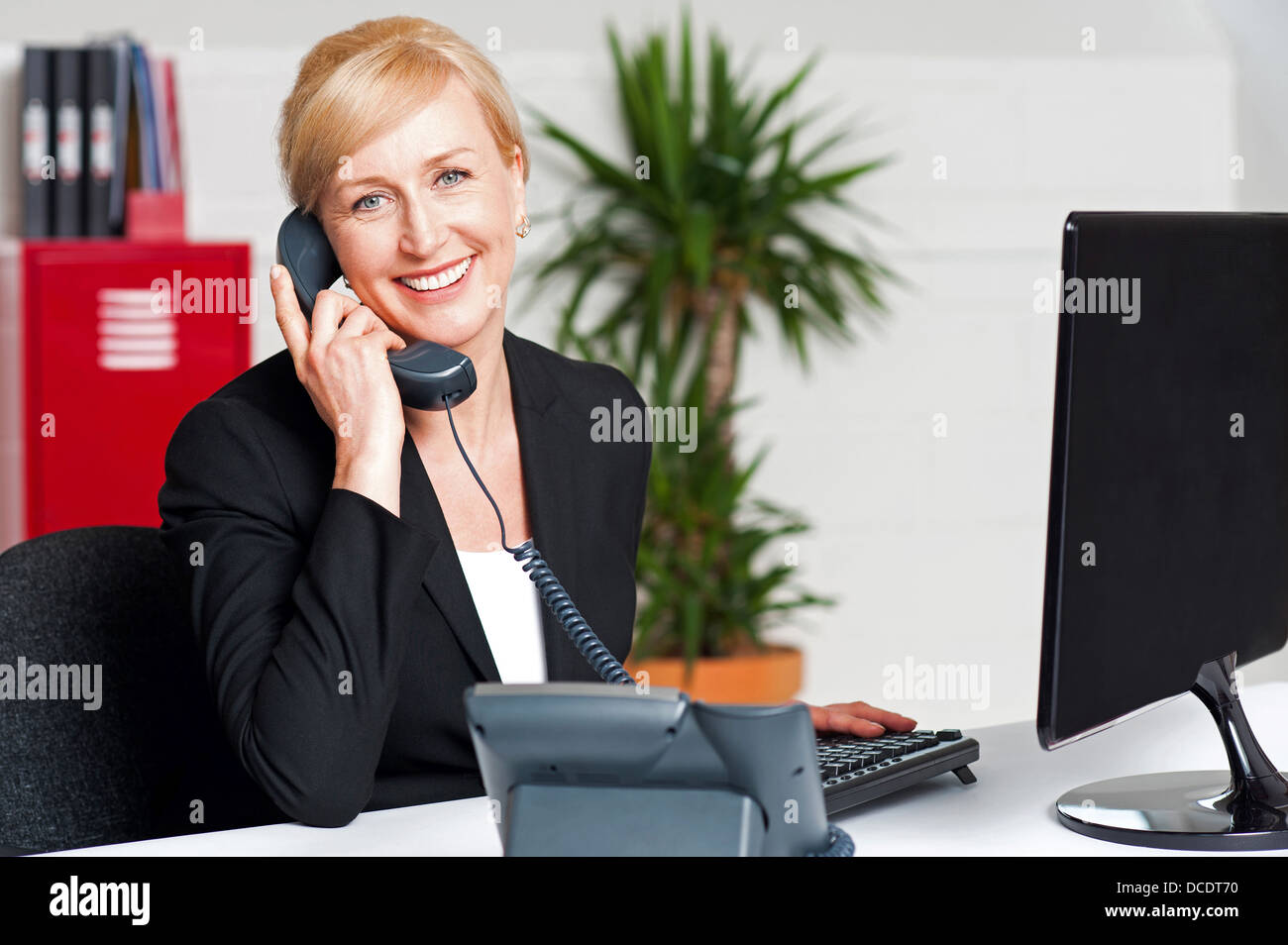 Secretary talking on phone with client, looking at you Stock Photo - Alamy