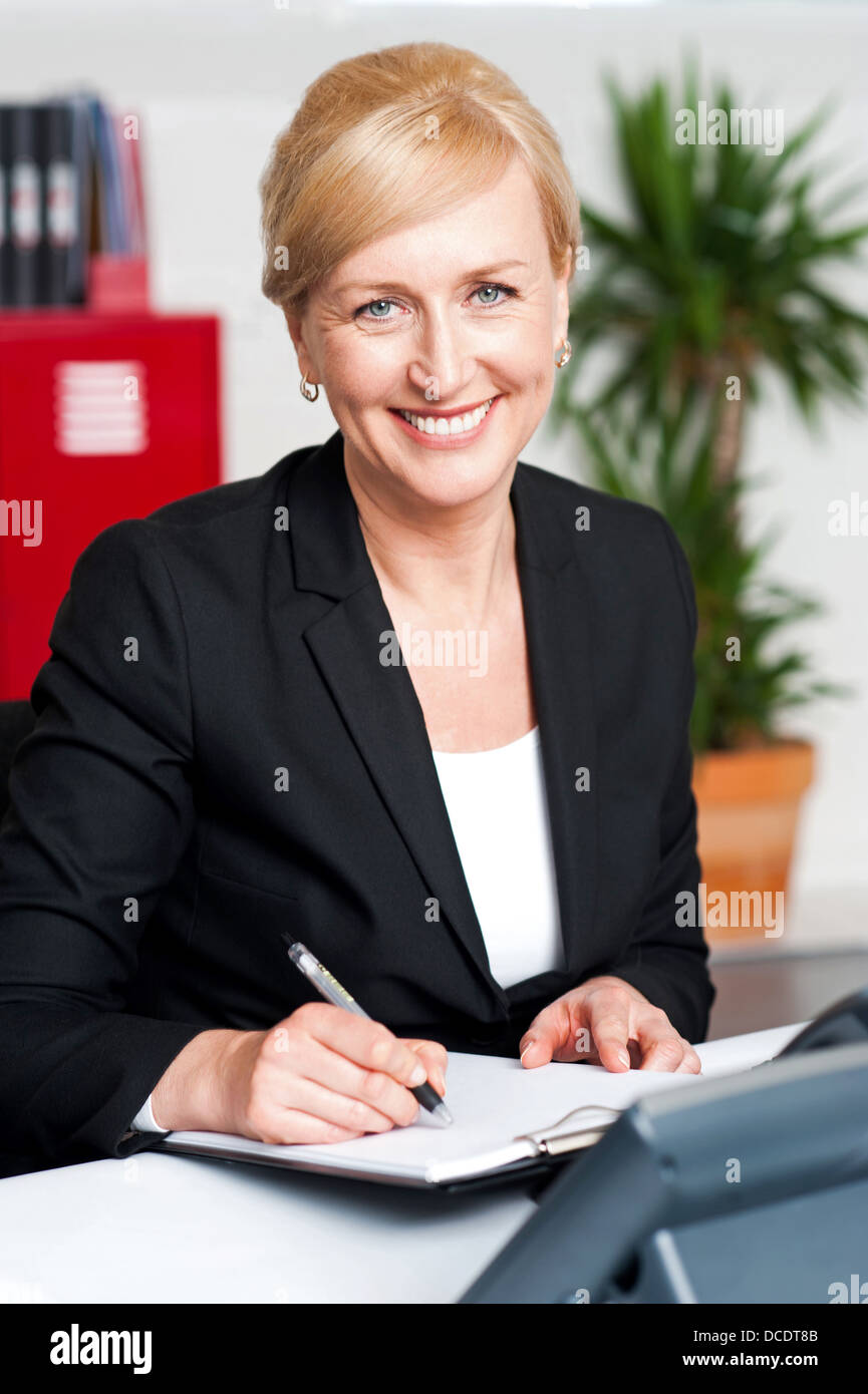 Seated female secretary writing on notepad in office and looking at you ...