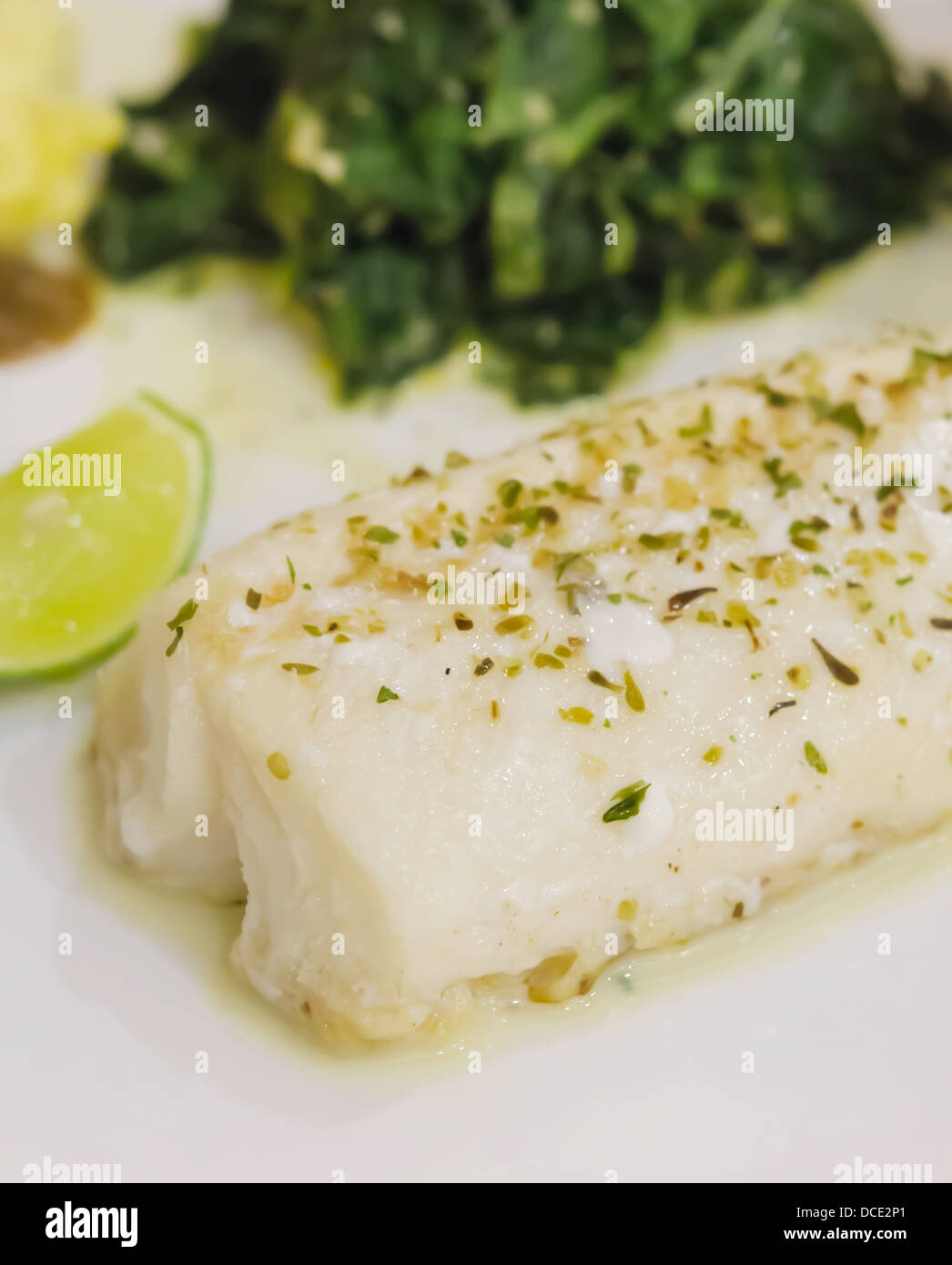 close up fillet fish steak with spinach and lime on white plate Stock ...