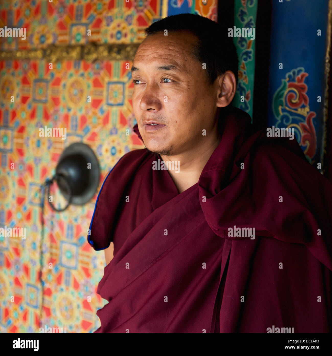 monk in red robe standing against, colorful wall at Drepung Monastery ...