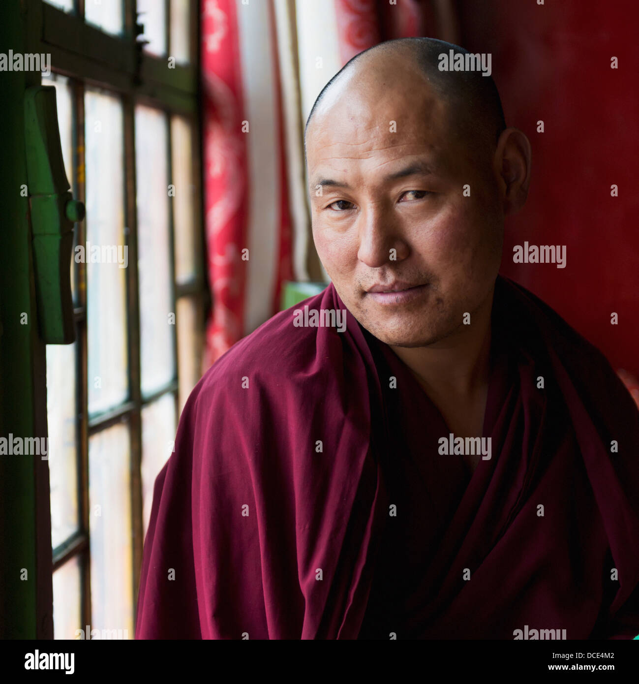 China, Xizang, Tibet, Portrait of, monk in, red robe sitting by, window ...