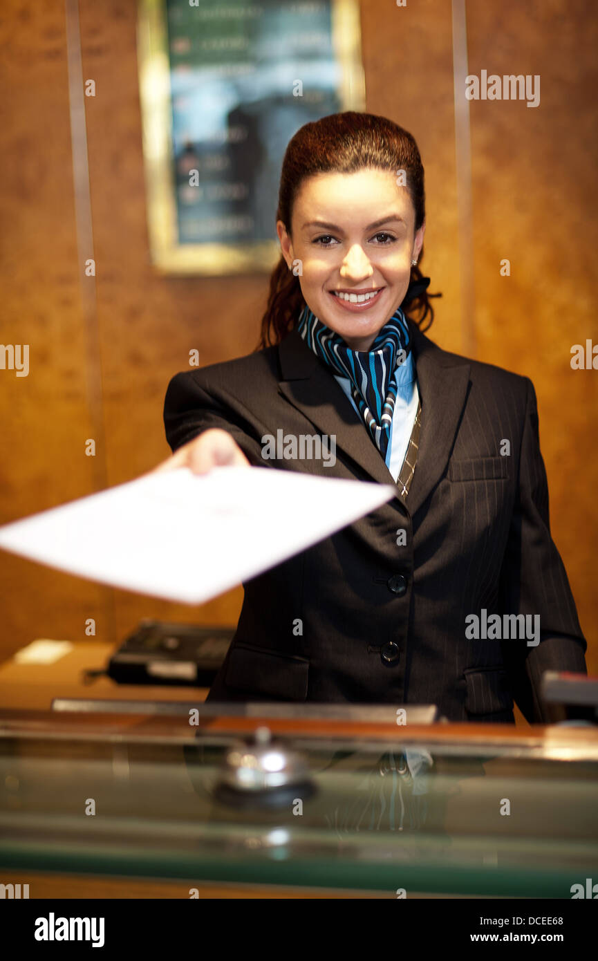Cheerful female receptionist offering check-in papers to the customer ...