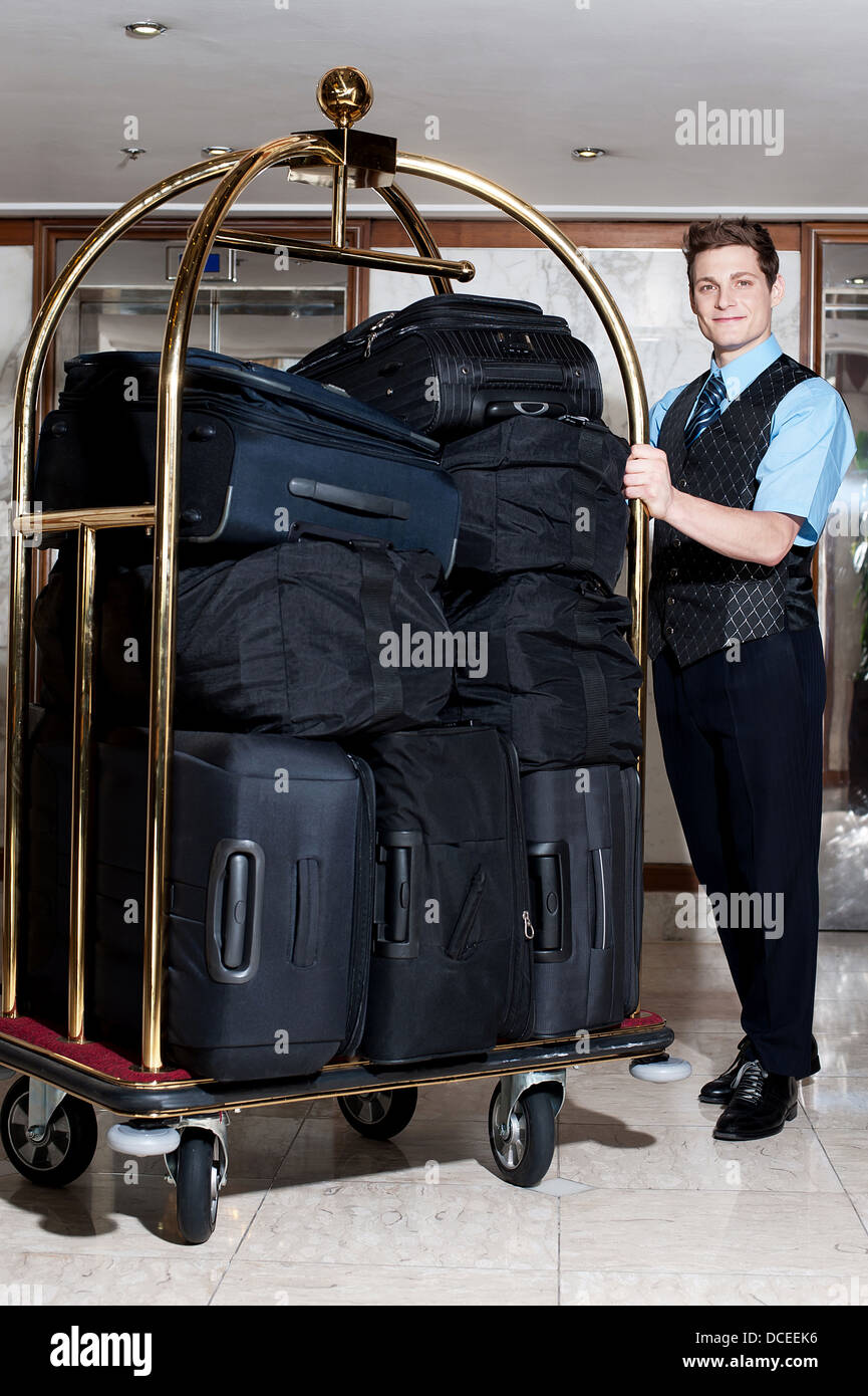 Handsome male concierge posing with a pile of bags in luggage cart ...