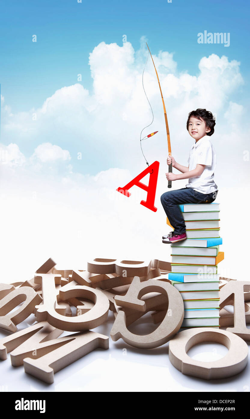 a boy sitting on a pile of book fishing alphabets Stock Photo - Alamy