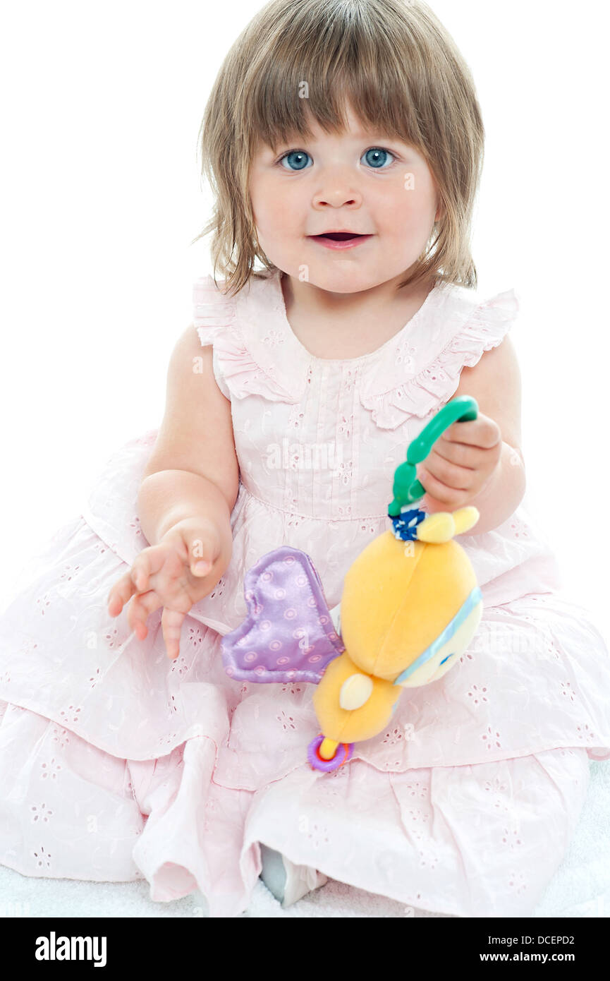 A cute little baby girl is looking into the camera while playing with ...