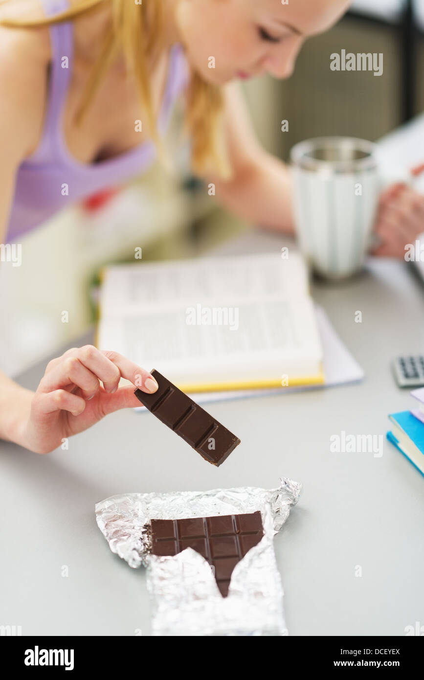 Closeup on teenager girl eating chocolate while studying in kitchen ...