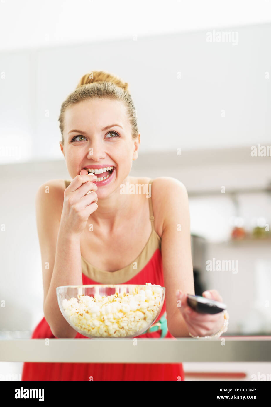 Smiling Young Woman Eating Popcorn And Watching Tv In Kitchen Stock