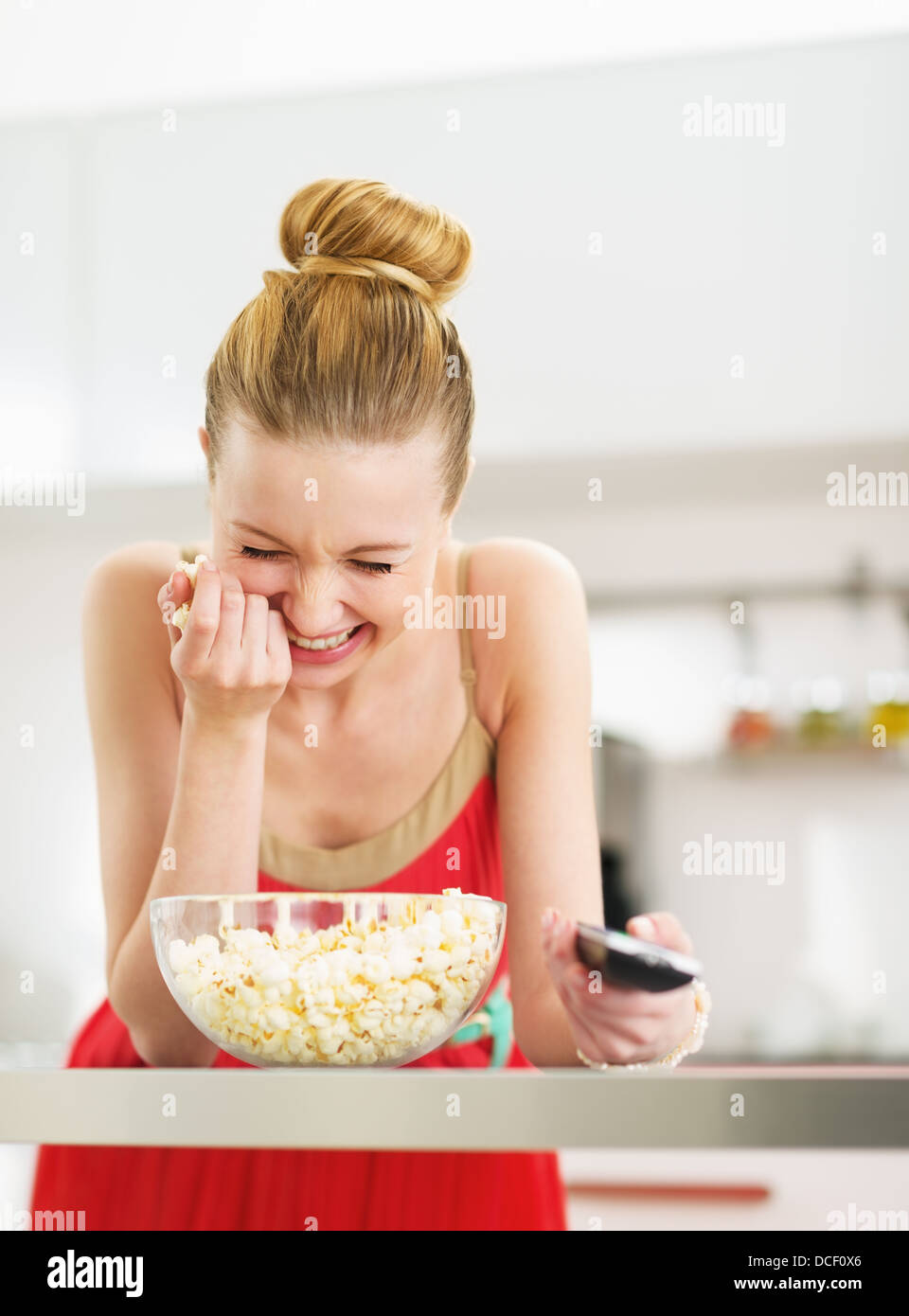 Laughing young woman eating popcorn and watching tv in kitchen Stock ...