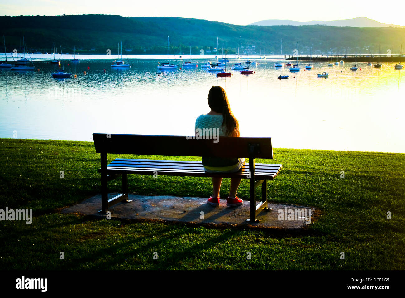 Young girl on park bench watching sunset over water Stock Photo - Alamy
