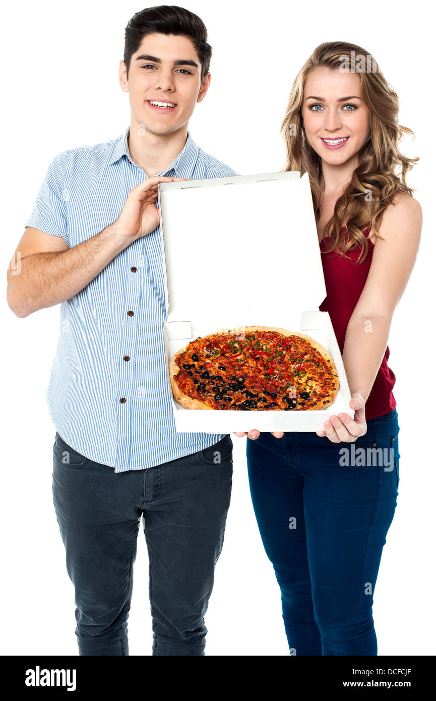 Young couple offering a medium sized delicious pizza to you Stock Photo ...
