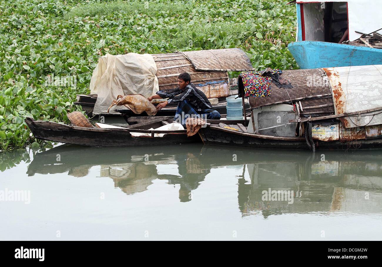 Bangladeshi river gypsy works on her boat as a boat man attempts to ...