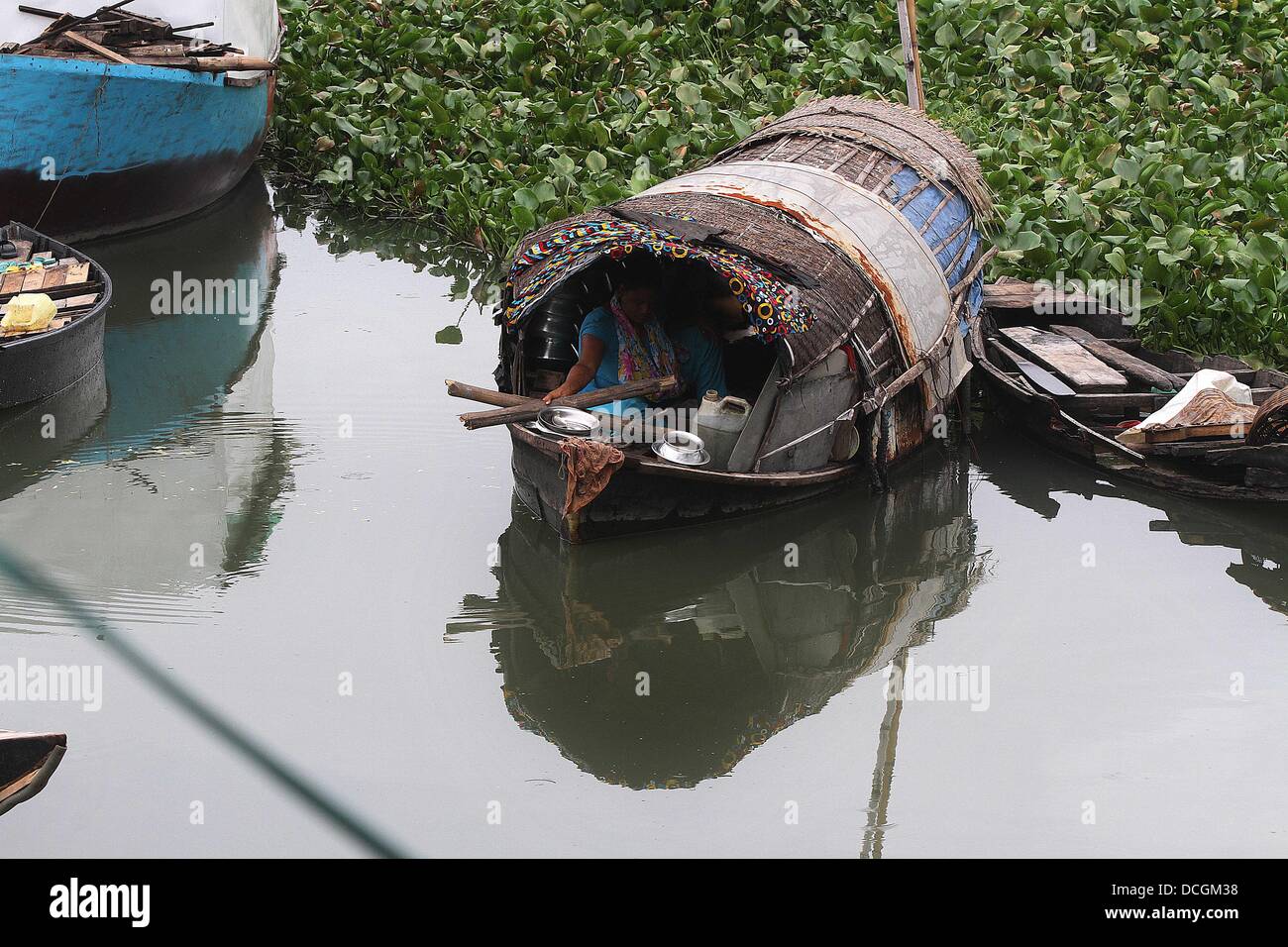 Bangladeshi river gypsy works on her boat as a boat man attempts to ...