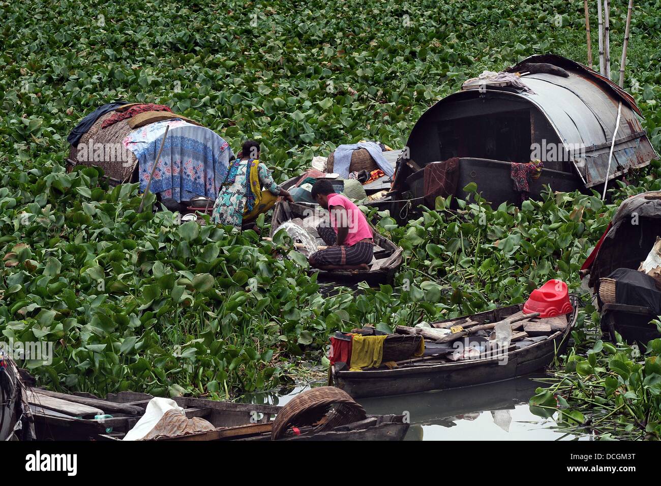 Bangladeshi river gypsy works on her boat as a boat man attempts to ...