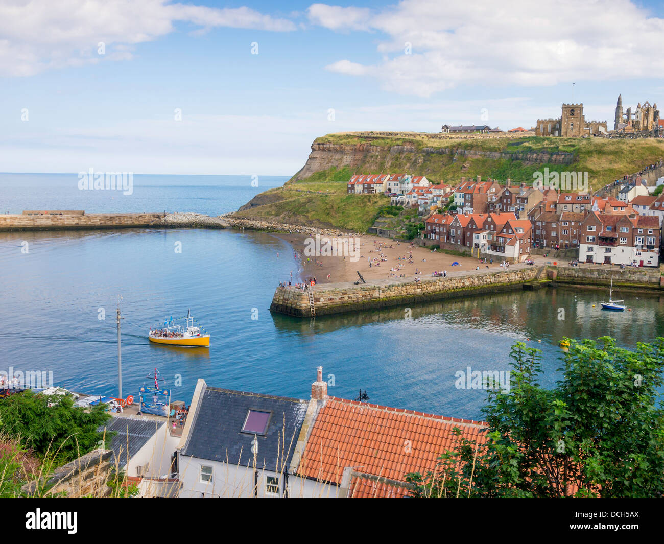 A pleasure boat entering Whitby harbour with cottages on the east side ...