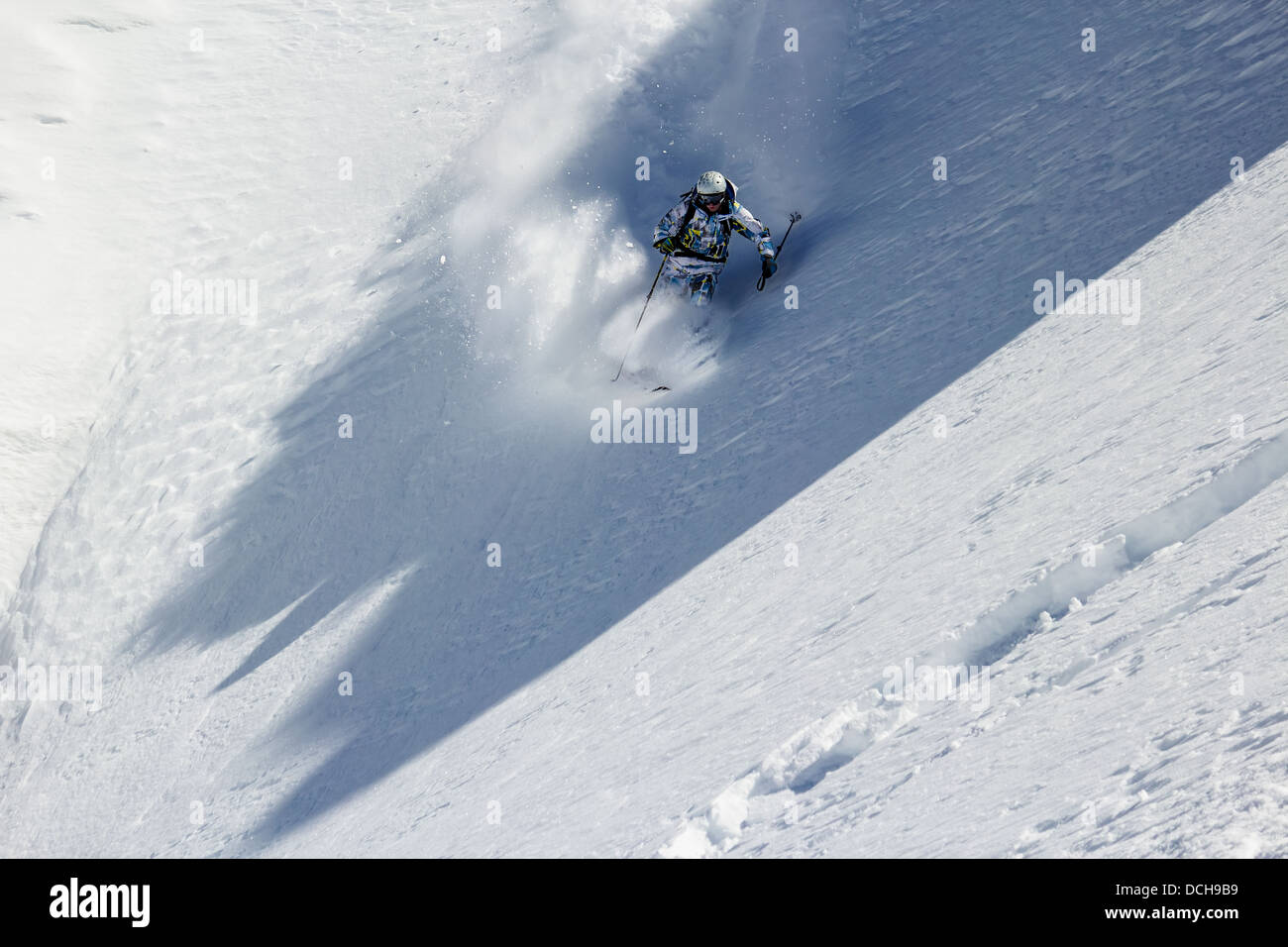 Skier raises snowy trail in a turn on a steep slope at the edge of ...