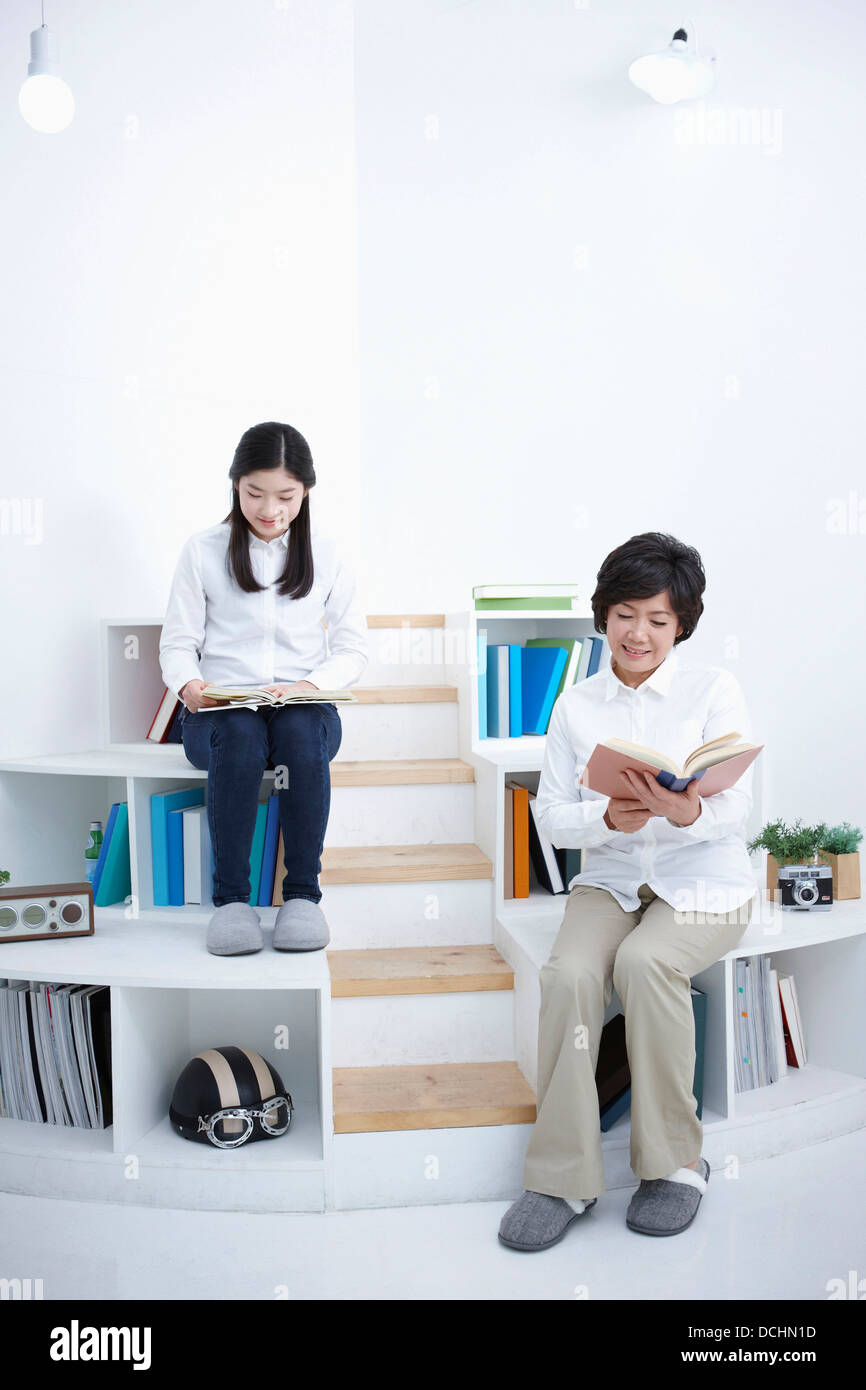 a student and mother sitting on bookshelf reading Stock Photo - Alamy