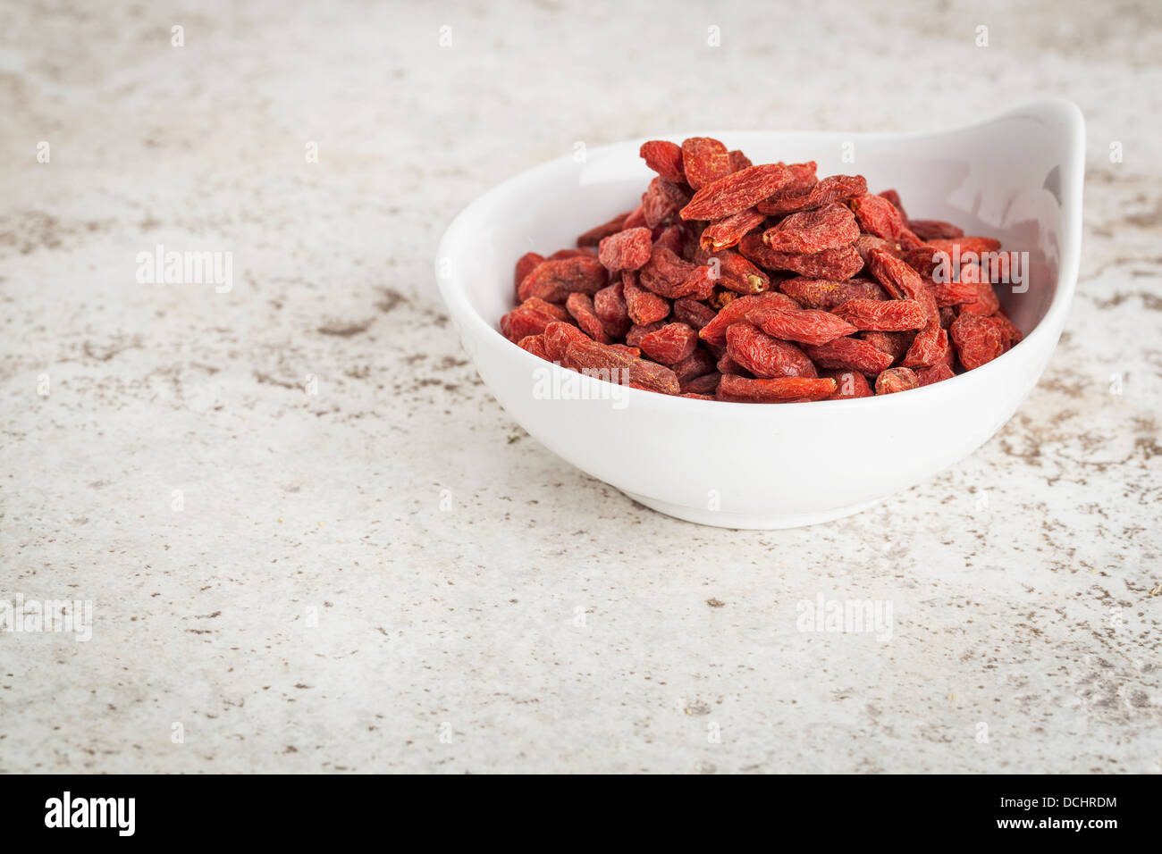 small ceramic bowl of dried goji berries against a ceramic tile ...