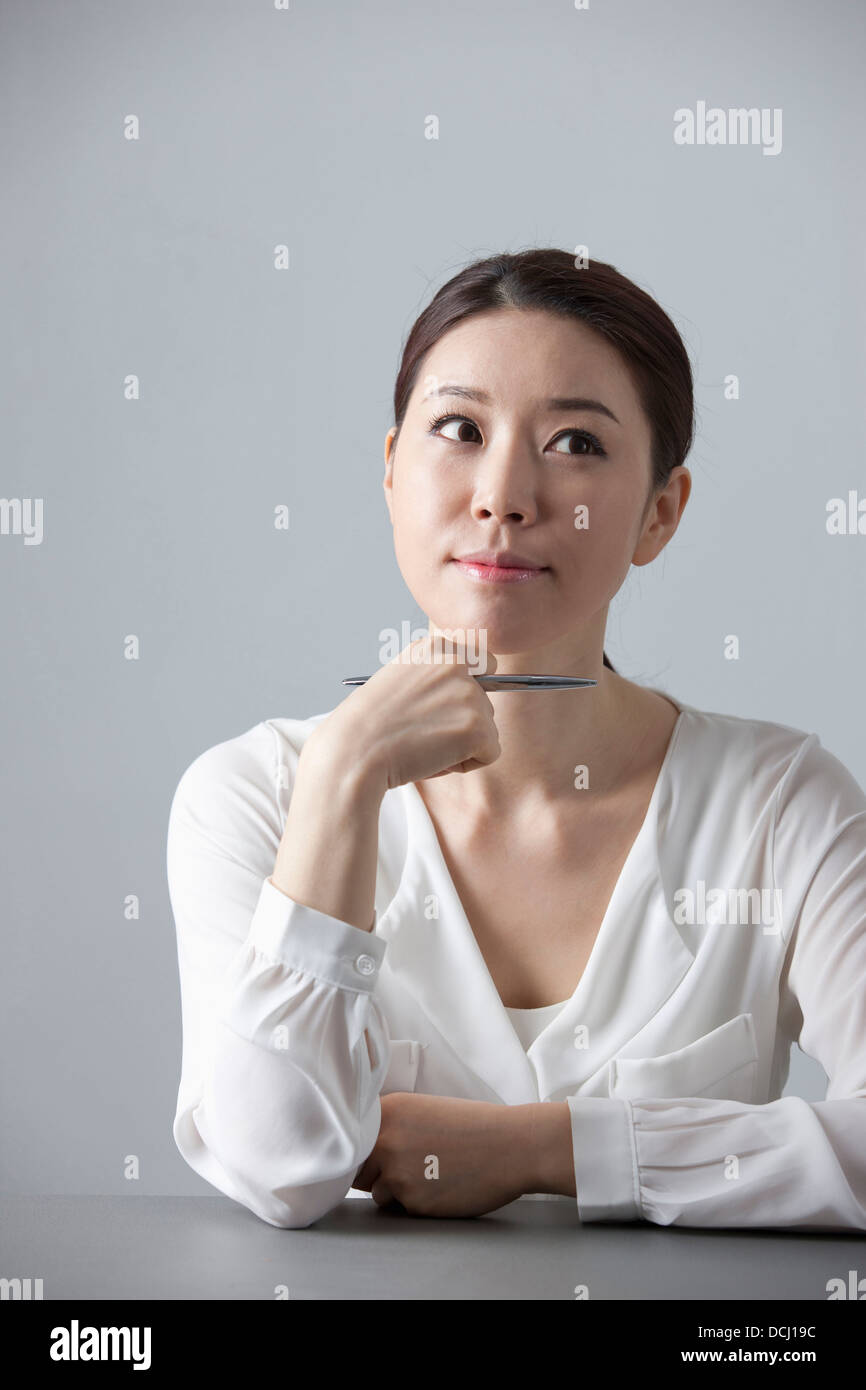 a woman thinking while sitting at a desk Stock Photo - Alamy